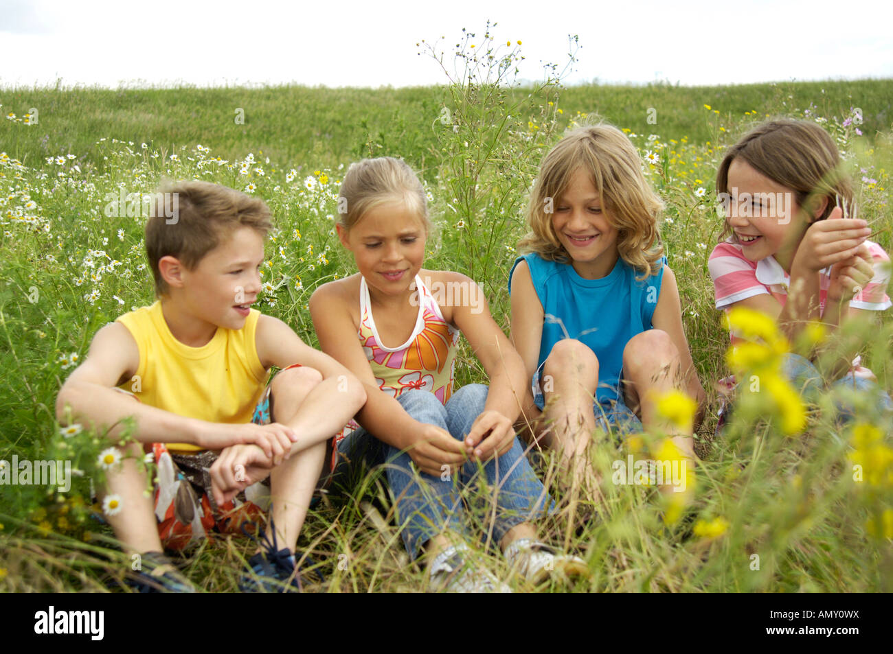 four children sitting in field and smiling Stock Photo - Alamy