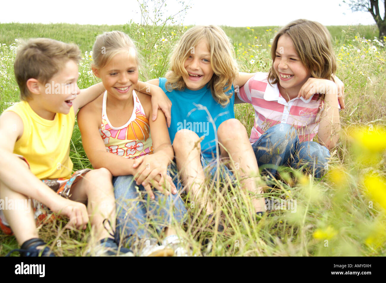 four children sitting in field and smiling Stock Photo - Alamy