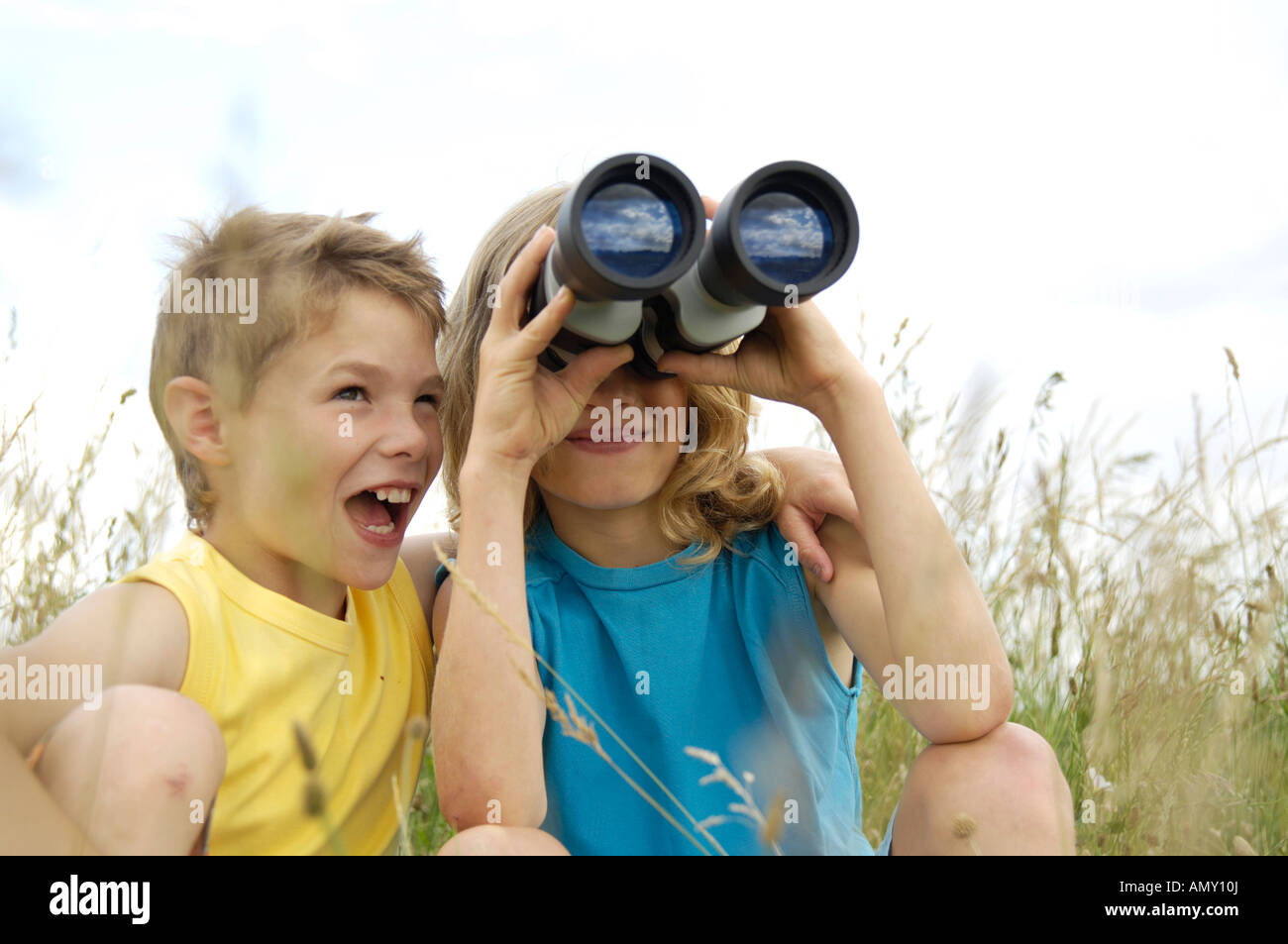 Boy looking through binoculars in field with his friend sitting beside ...