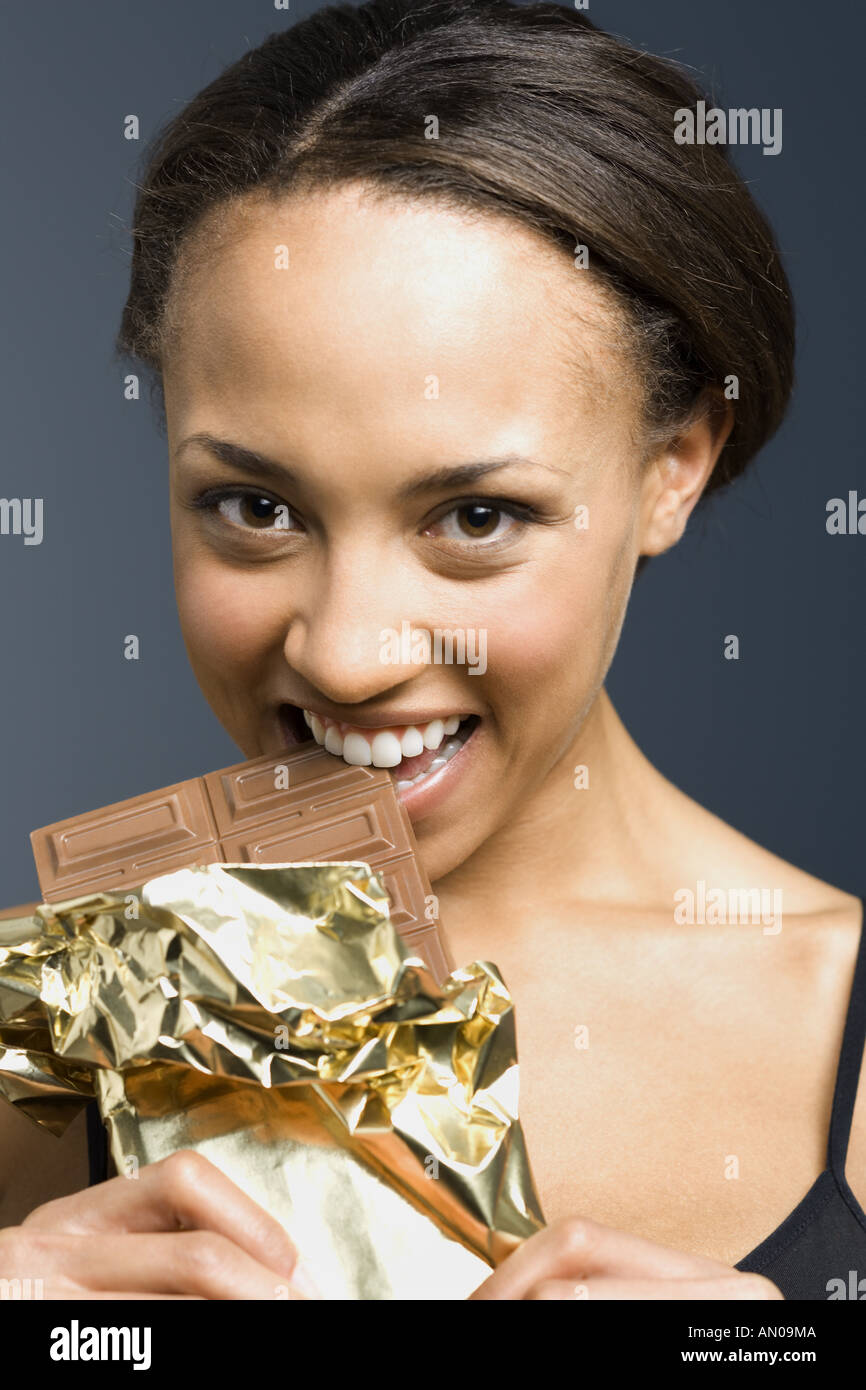 Portrait of a young woman biting into a bar of chocolate Stock Photo ...
