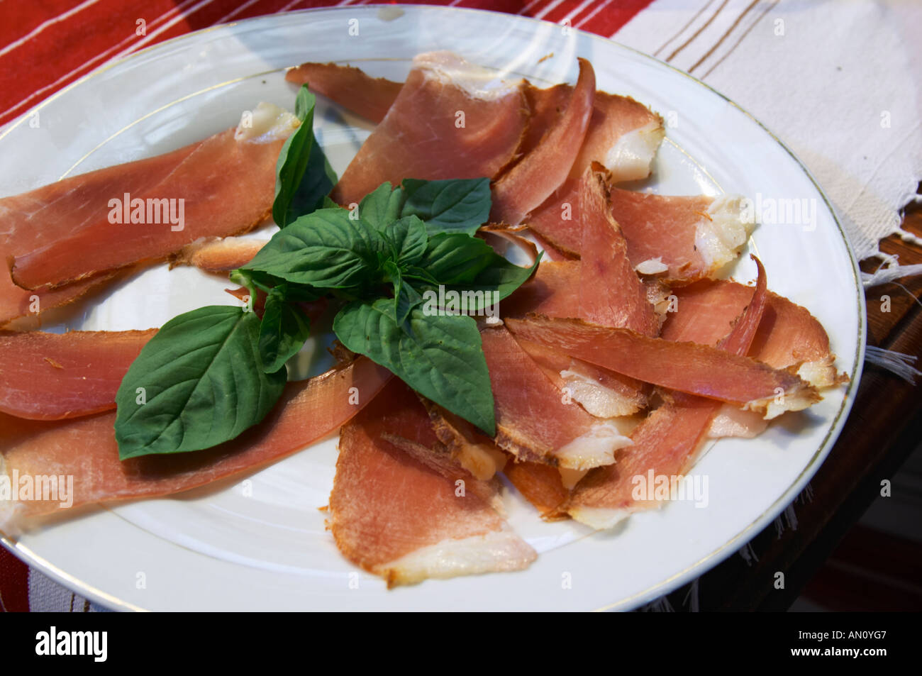 Dried dry cured ham with basil leaves on a white plate. Tradita ...