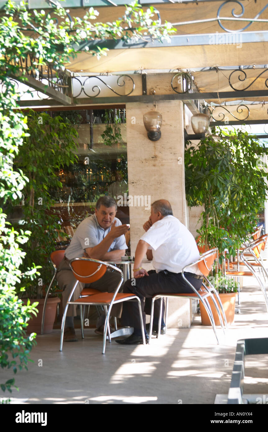 Street scene, men sitting at a cafe drinking coffee in the shade ...