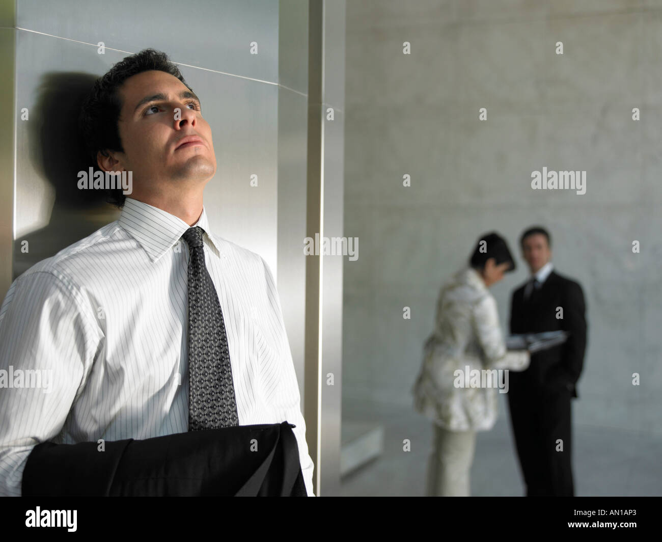 Man leaning up against a lift door with a jacket hanging over his arm ...