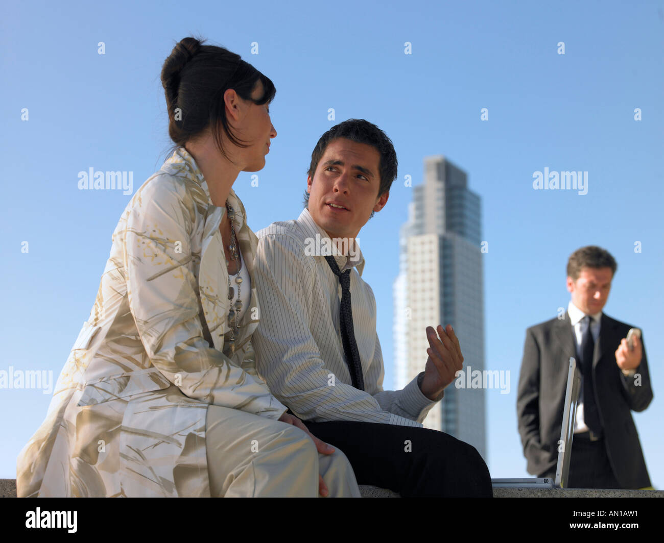 Two people talking whilst one standing with a phone Stock Photo - Alamy