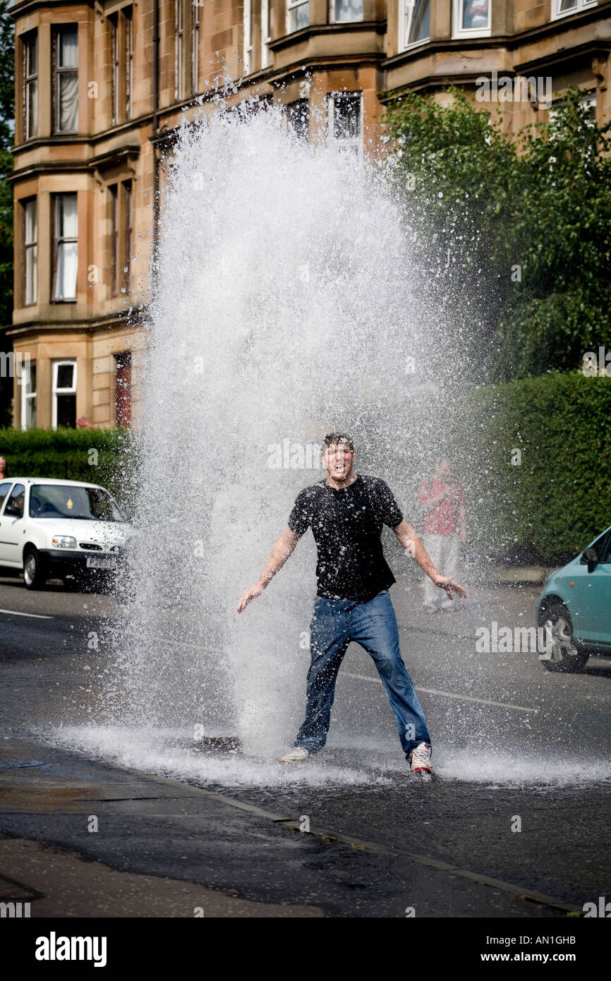 A young man cools down in the summer heat as a main water hydrant burst ...