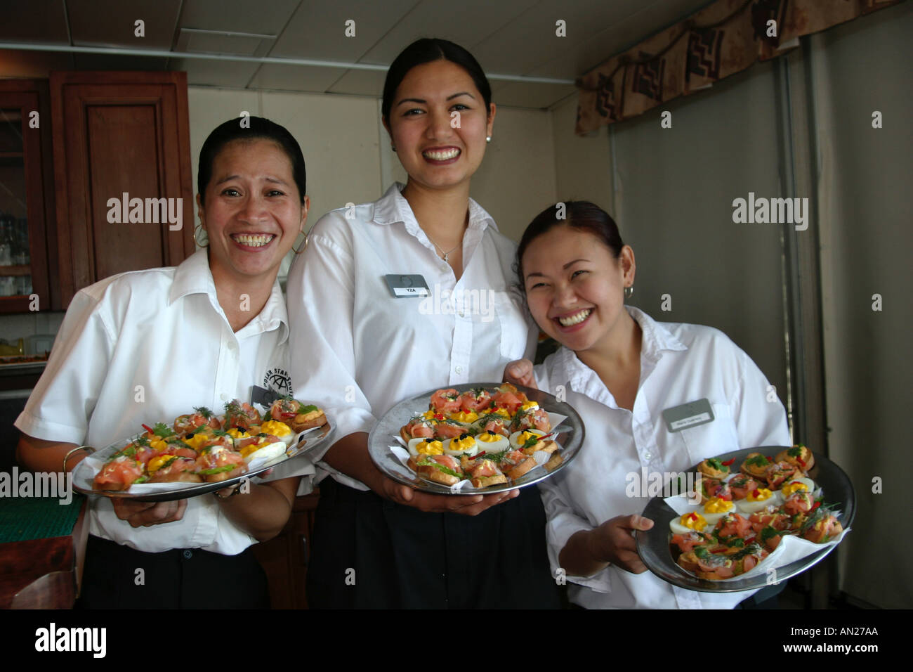 Three laughing Filipino waitresses holding trays of canapes on board a ...