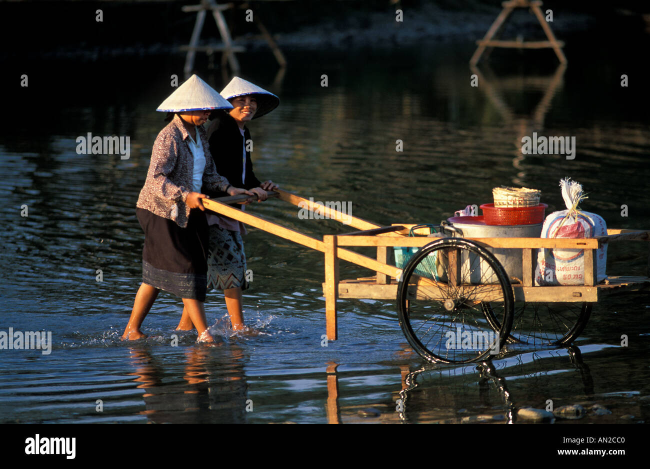 Women pushing trading cart through shallow waters of river Vang Vieng ...