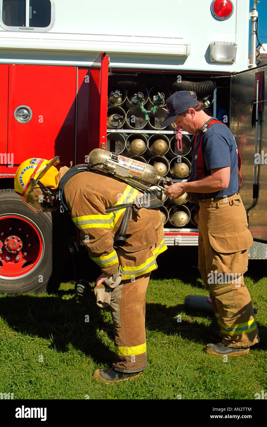 Two firefighters help each other get in their gear to prepare to battle ...