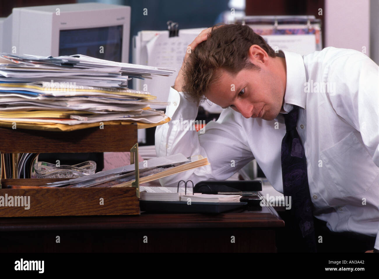 Stressed male office worker sitting at desk with piles of Paperwork ...