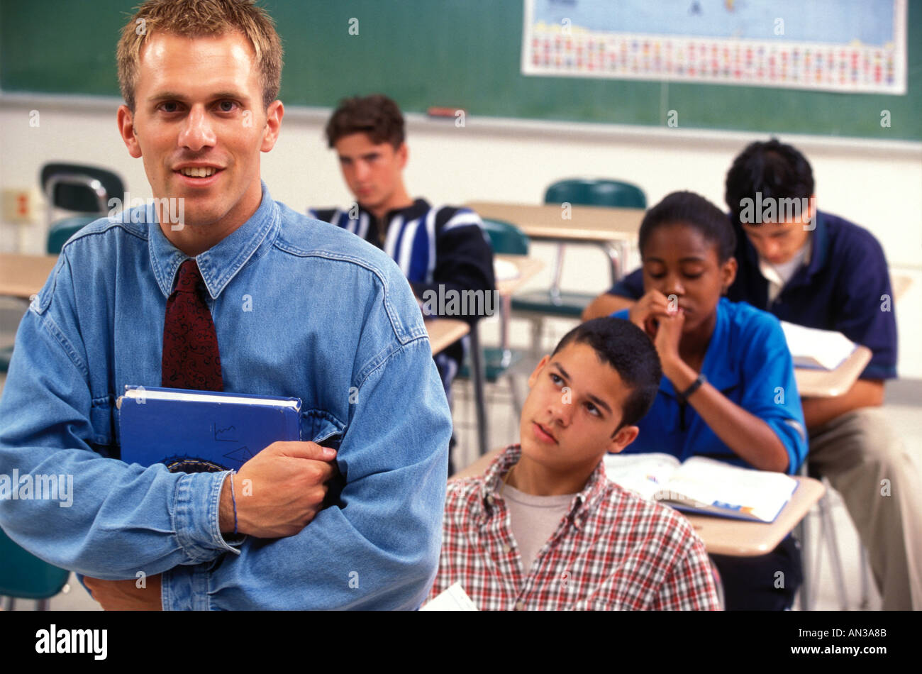 Portrait of high school teacher in classroom with students working at ...