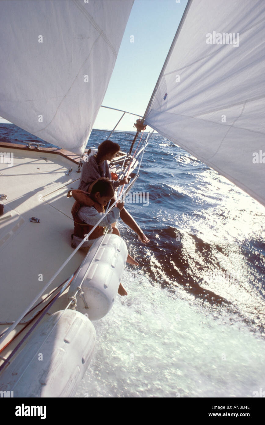 Caucasian brother and sister sitting on sailboat railing trailing feet ...