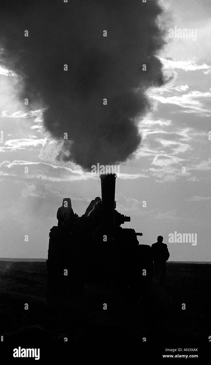 Silhouette of steam traction engine making smoke against a brightly lit ...