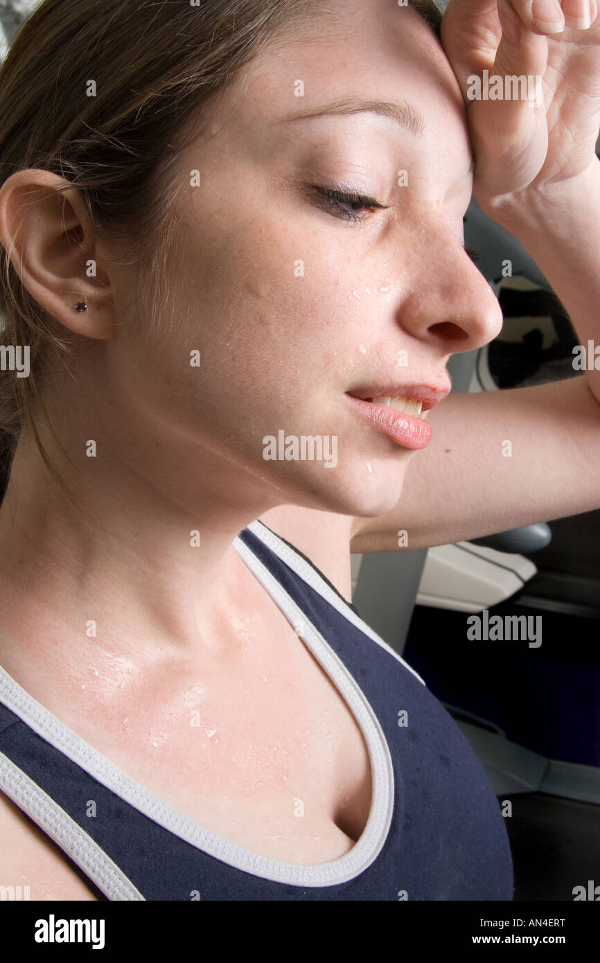 Tired young woman mopping sweat or perspiration from her brow after ...