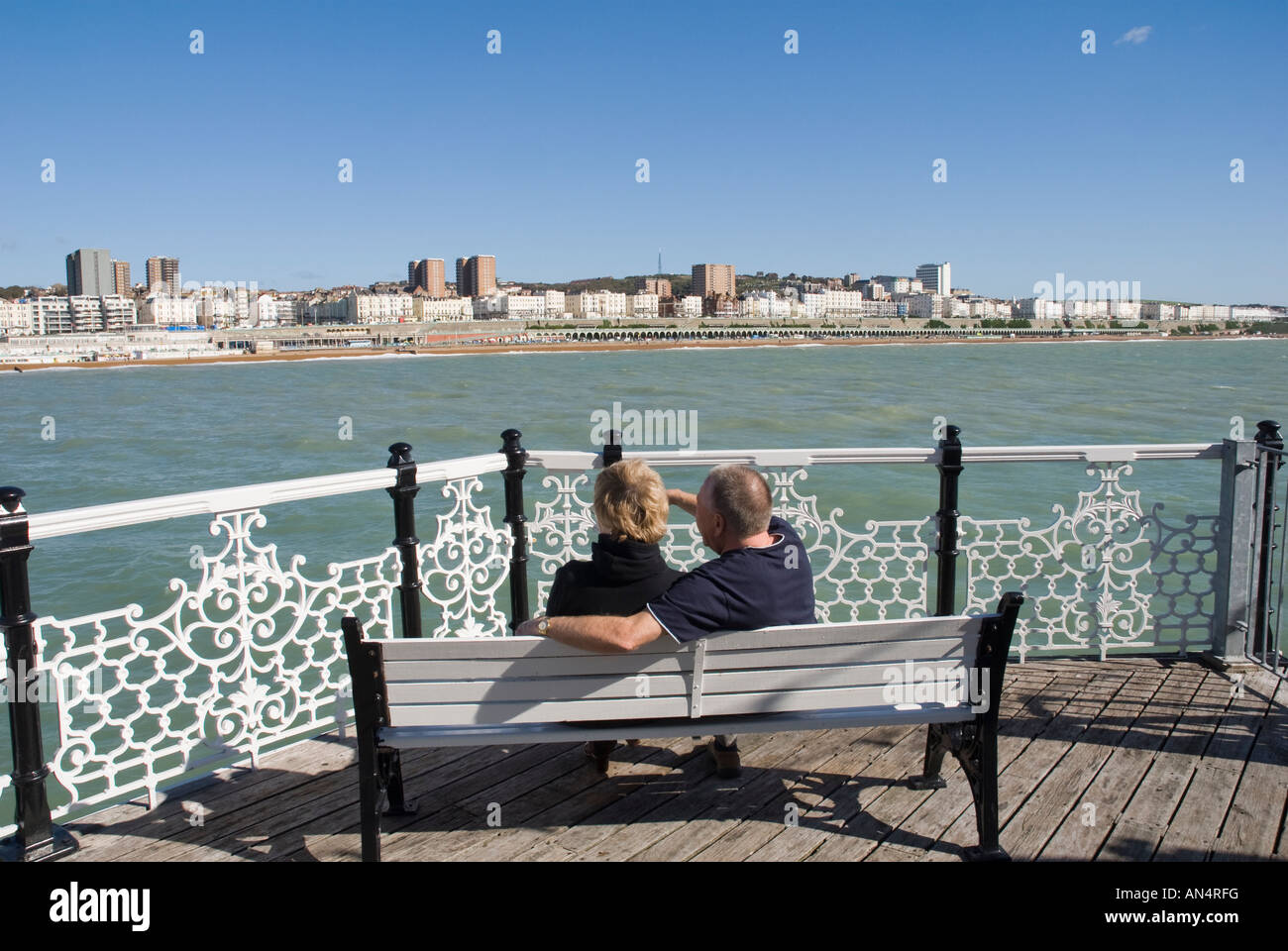 Two people sitting on a bench on Brighton pier looking towards the city ...