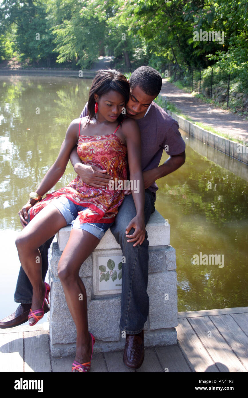 An African American couple are sitting on a post by a lake in the ...