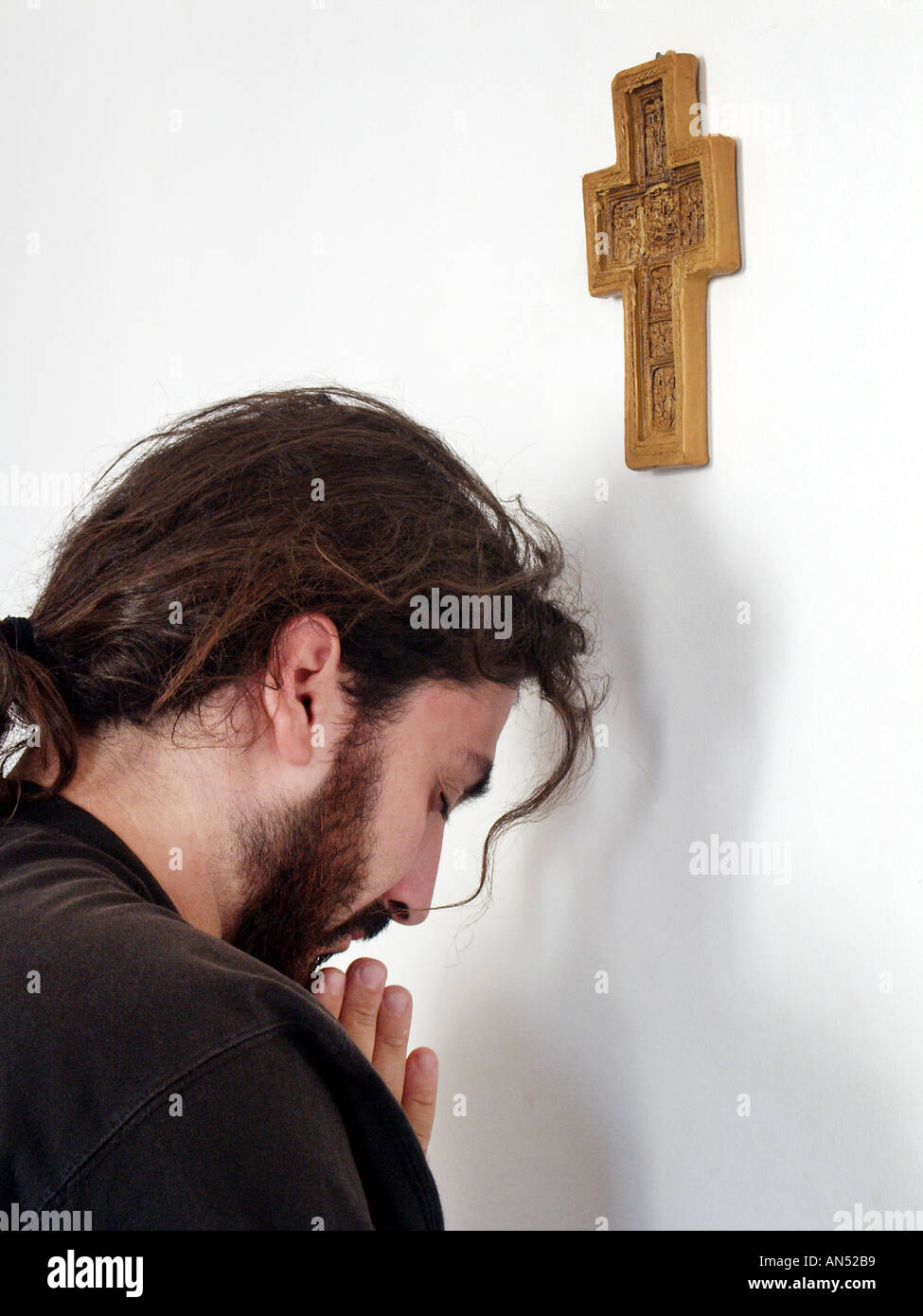Praying man under Christian Cross hanging on wall Stock Photo - Alamy