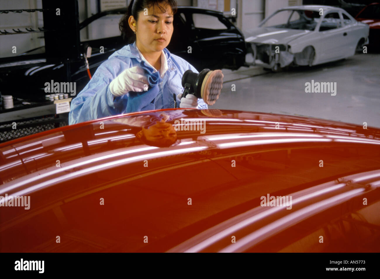A female assembly line worker buffs the paint finish on a new car at ...