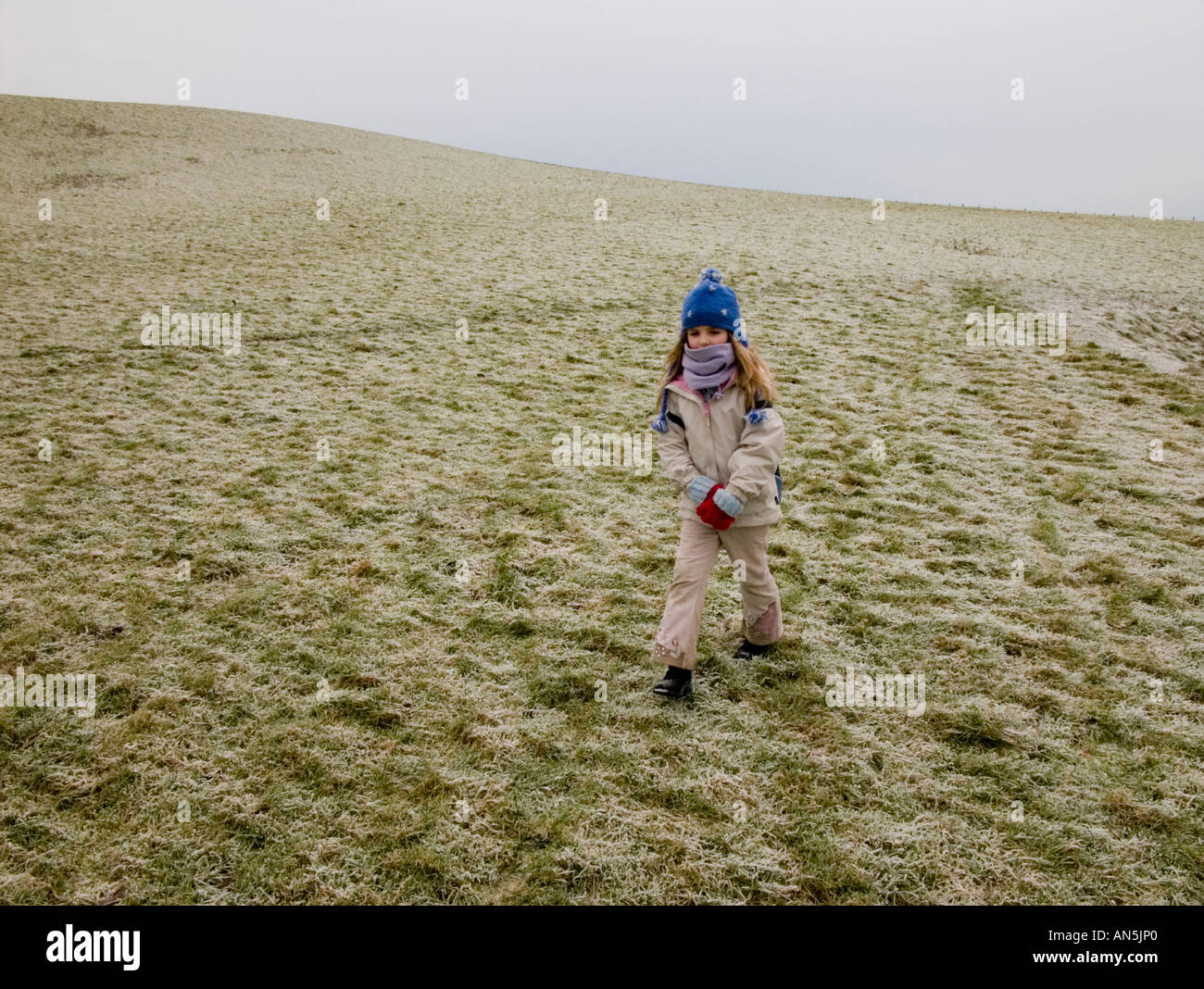 Young girl wrapped up warm in her winter coat and blue hat walking ...