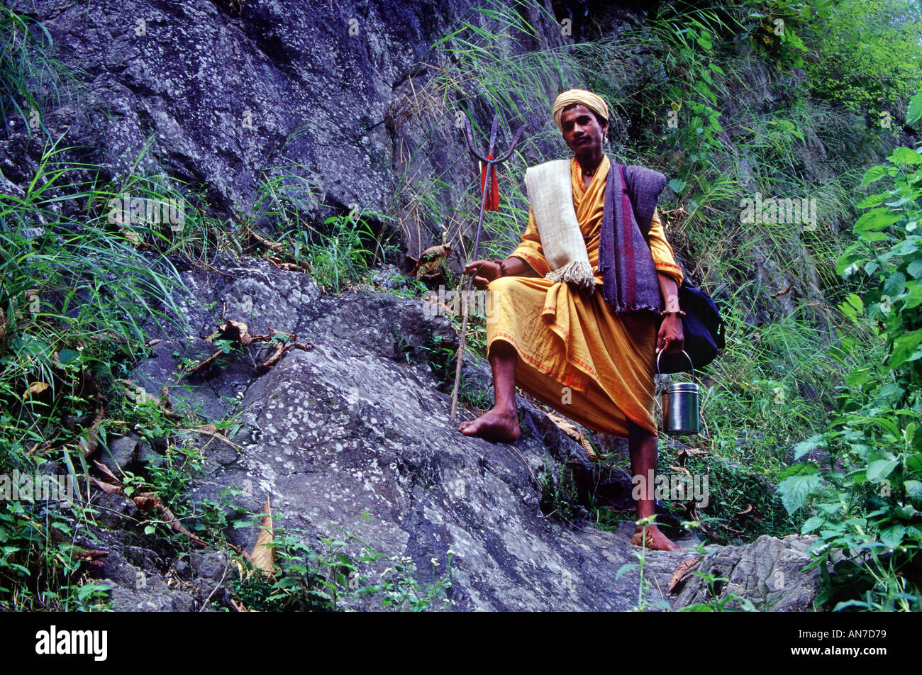 Young sadhu in traditional clothes climbing the rocks with bare feet ...