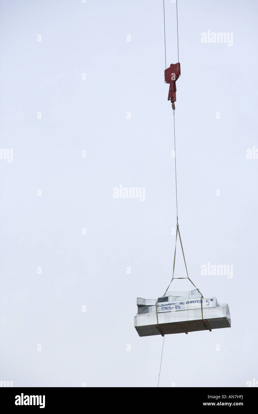 A crain at a construction site lifts building material to the top of a ...