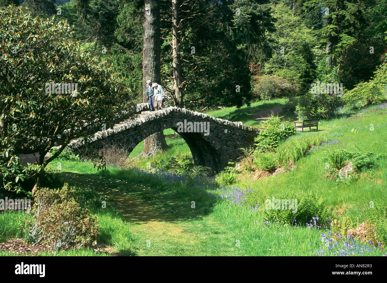 An elderly couple walk across an old stone bridge over a stream through ...