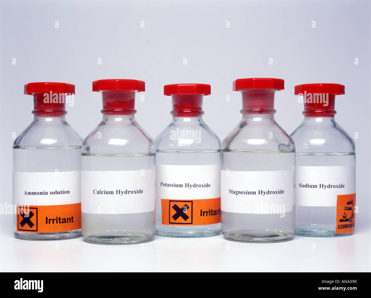bottles of some soluble hydroxides with hazard labels against a white ...