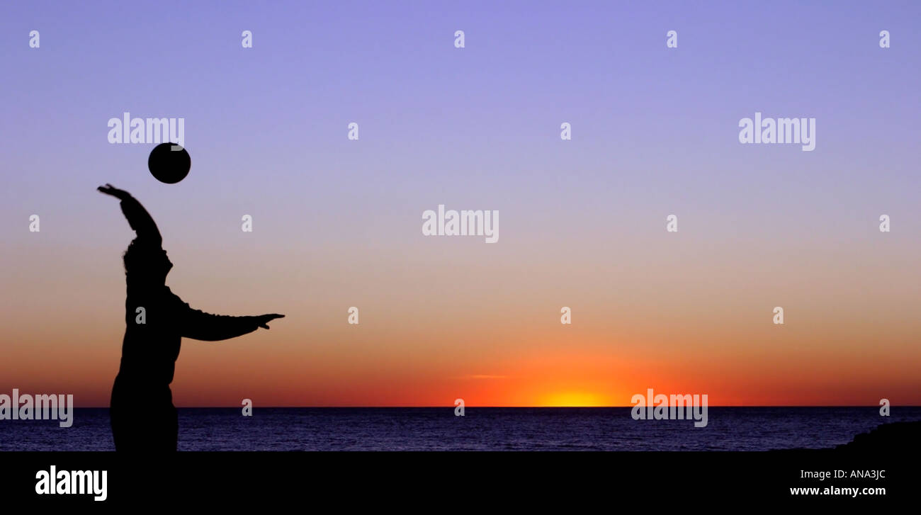 A volleyball player serves the ball as the sun sets into the Pacific ...