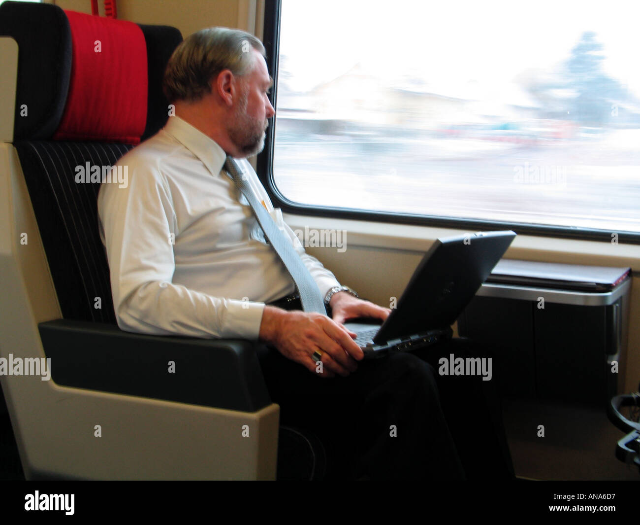 Businessman with laptop computer seated in train cabin looking through ...