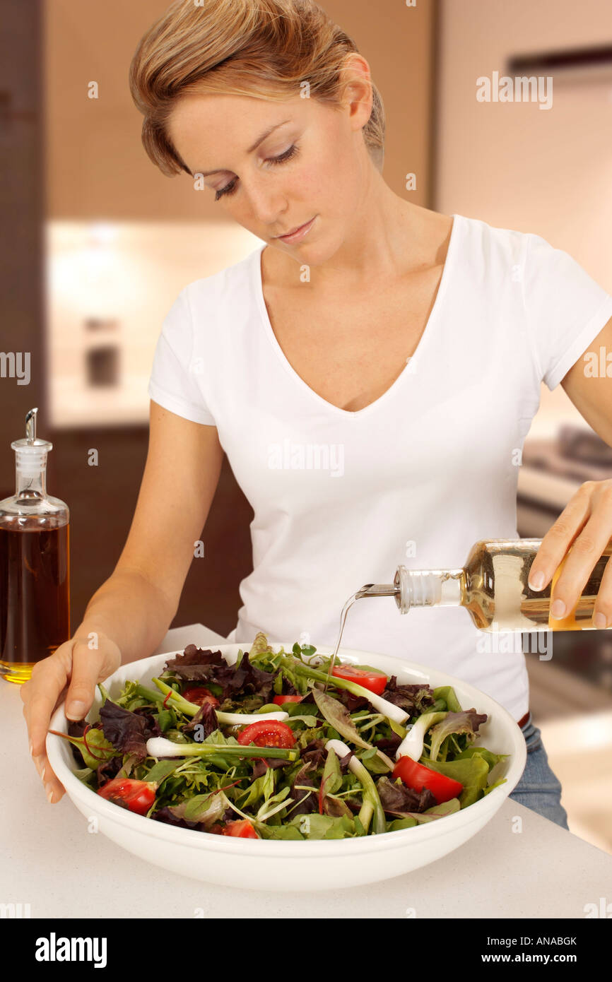 WOMAN IN KITCHEN POURING SALAD DRESSING ON SALAD Stock Photo - Alamy