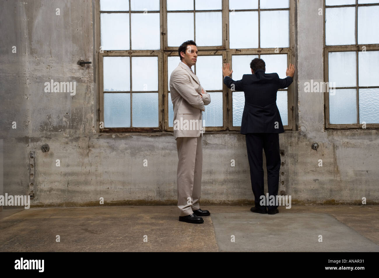 two businessmen standing in empty factory building one looking out of ...