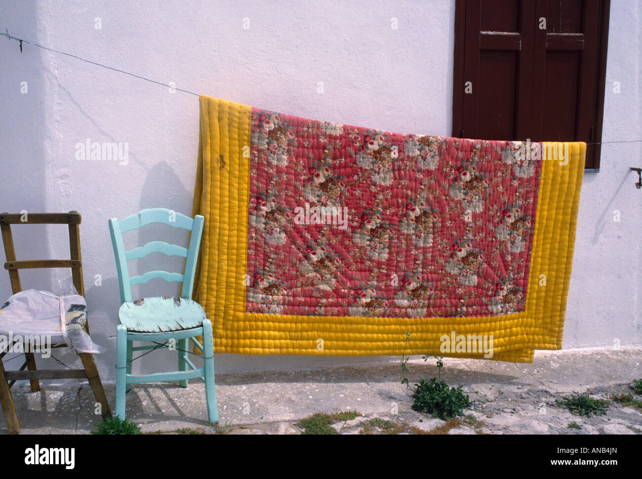 Wooden chairs beside yellow and red quilt on washing line in front of ...