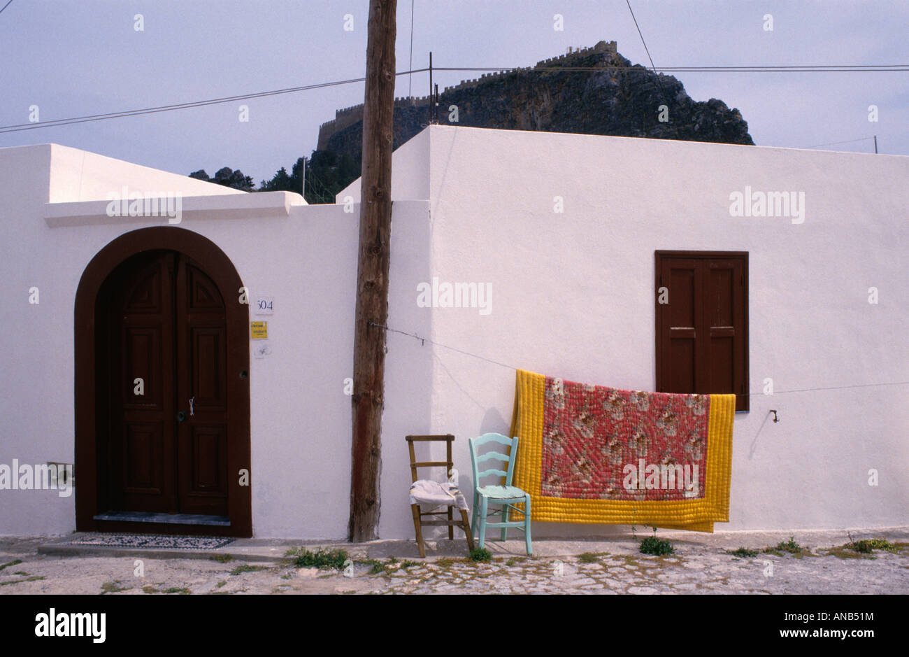 Wooden chairs and quilt on washing line outside small white Greek house ...