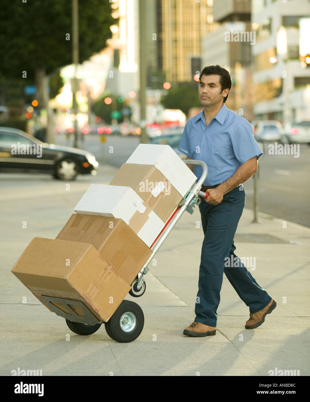 Hispanic delivery man walking on city sidewalk with hand truck full of ...