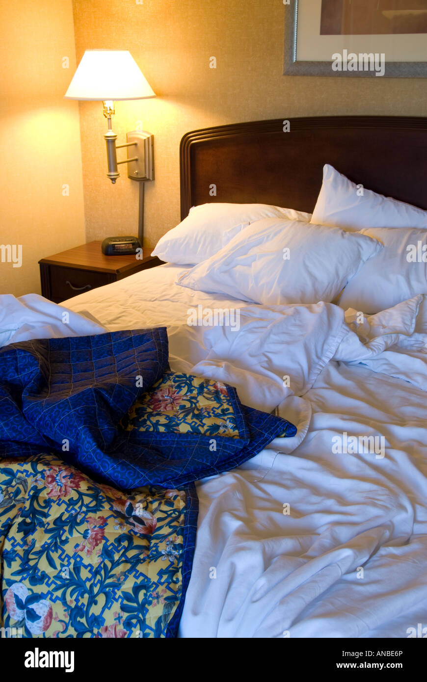 cropped view of unmade king sized hotel room bed with lighted wall lamp ...