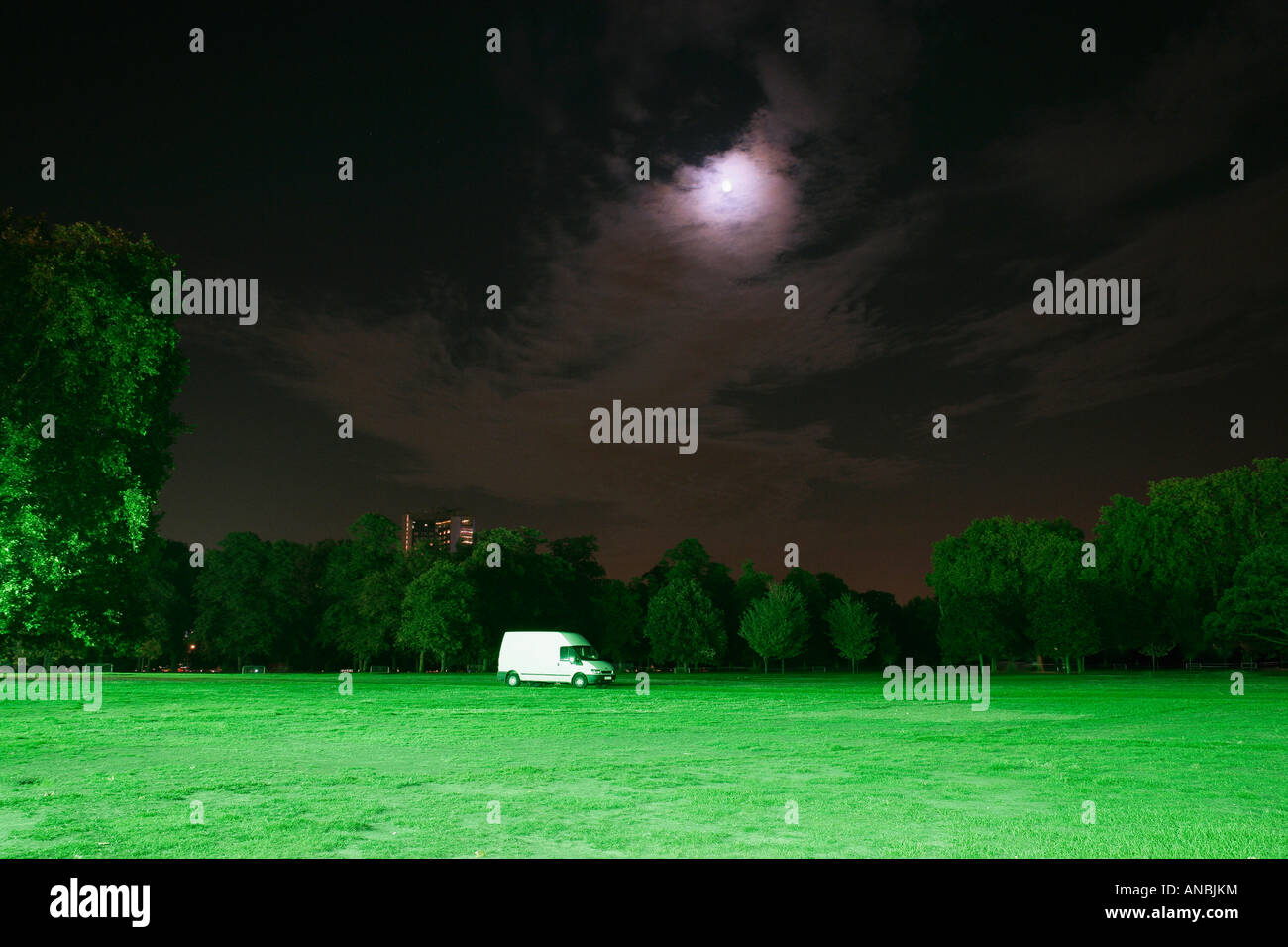 Park at night lit by green light with the moon breaking throught the ...
