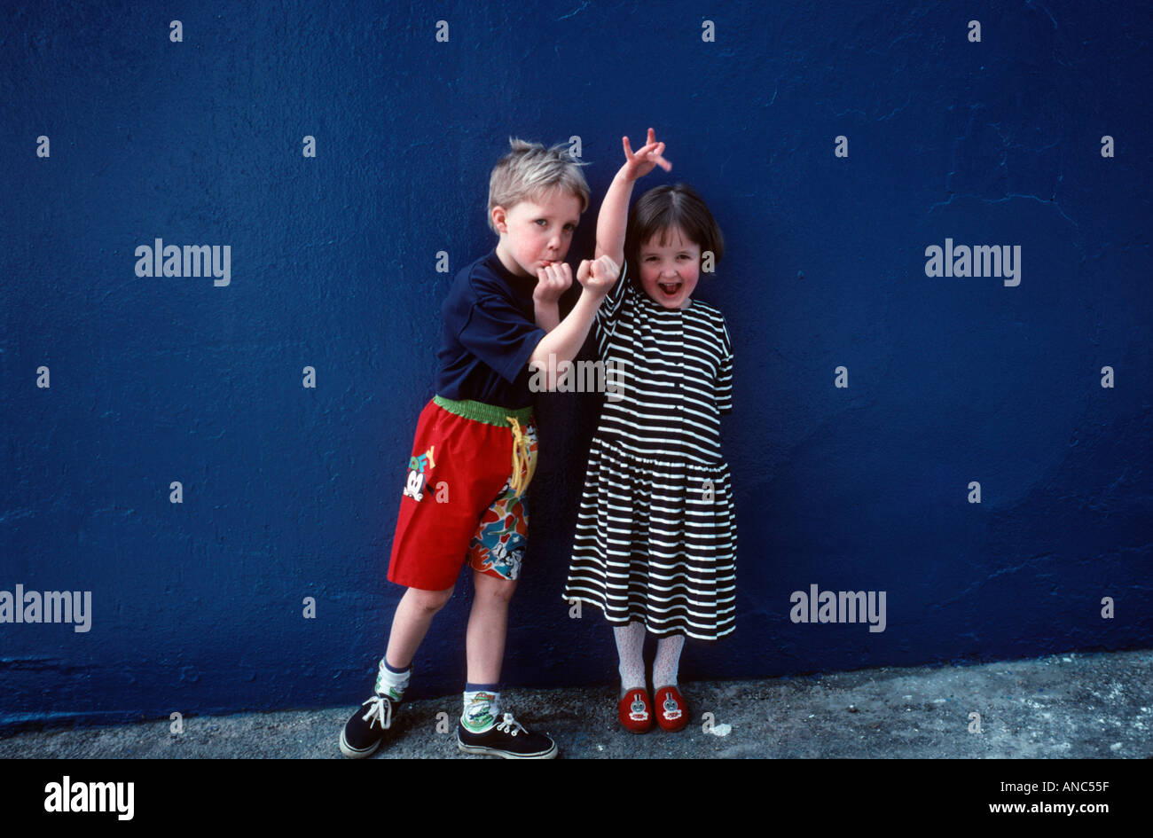 Small girl and boy standing in front of a deep blue wall and pretending ...
