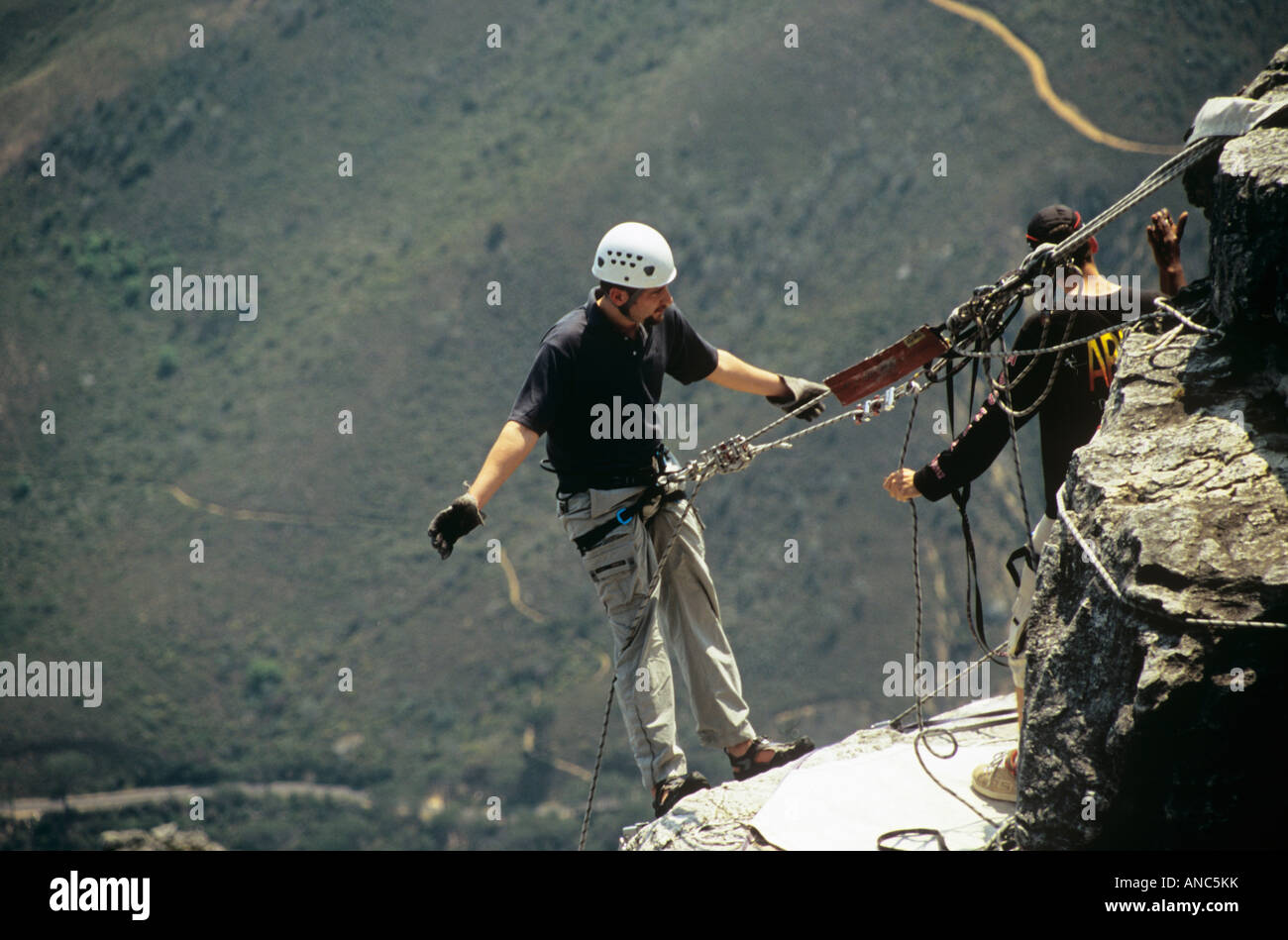 Man starting abseil off Table Mountain on rock edge with climbing rope ...