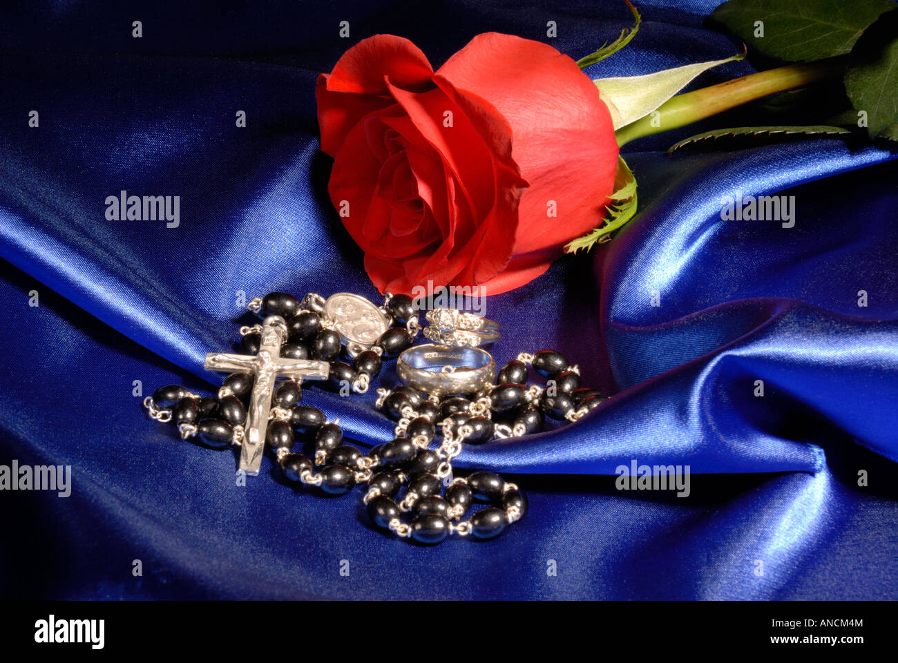 Wedding rings and rosary on blue satin with a rose Stock Photo - Alamy