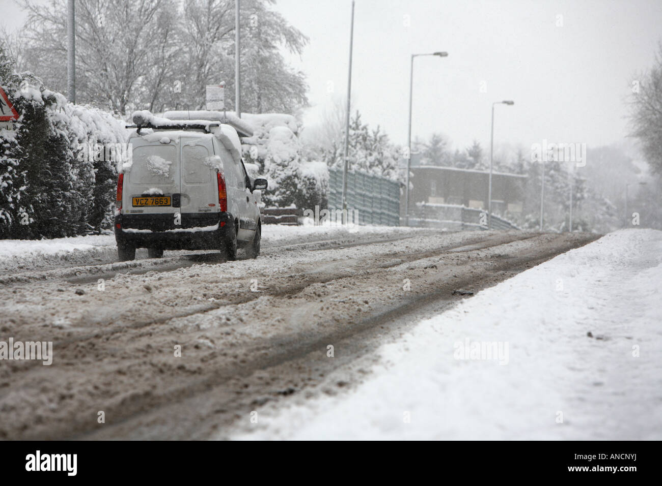white van driving slowly uphill on gritted salted lying snow turning to ...