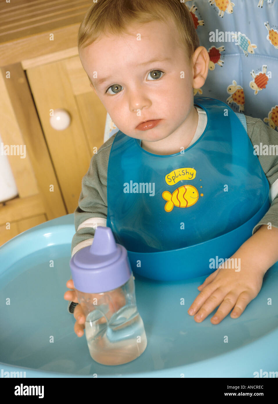 Young boy sitting down in a high chair drinking water from a beaker ...