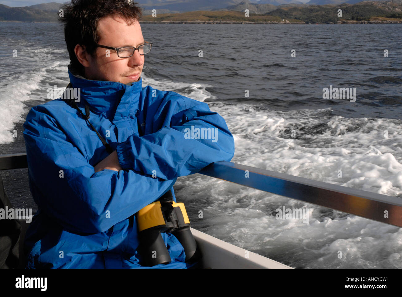 Man looking over the side of a boat with binoculars around his neck ...