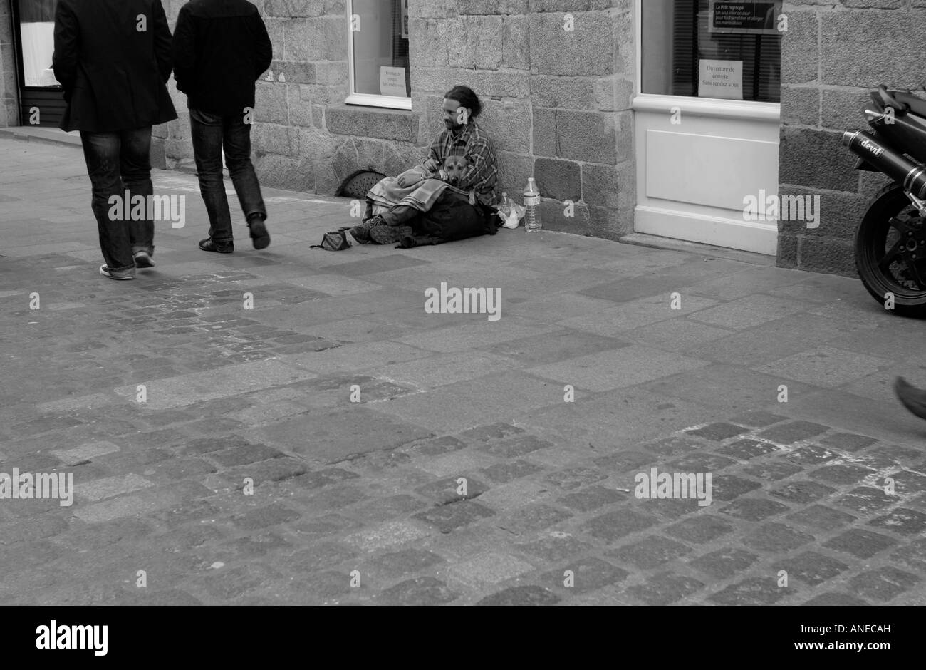A beggar with dog eying two passing men in a provincial French city ...