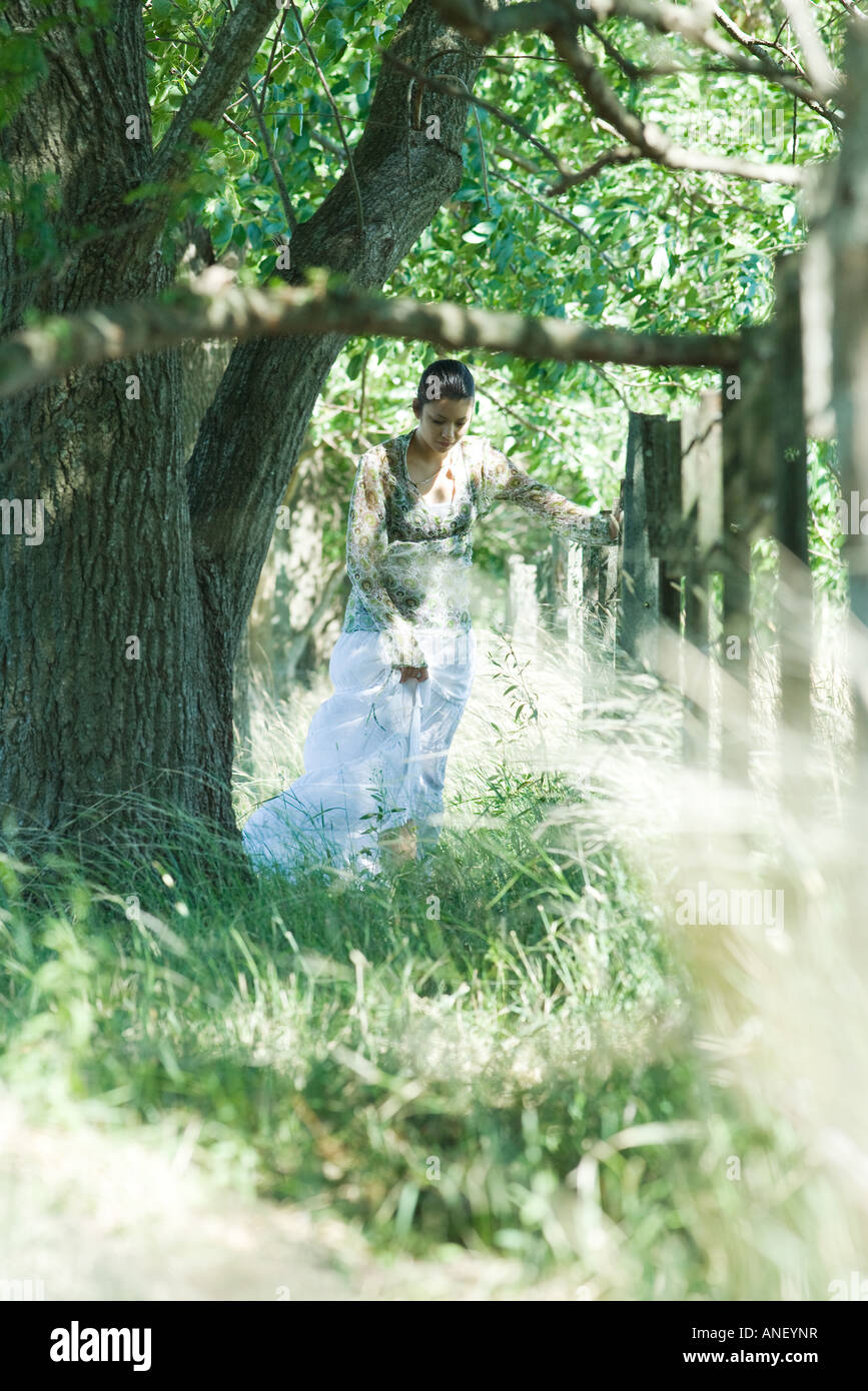 Young woman standing under tree, holding on to fence Stock Photo - Alamy