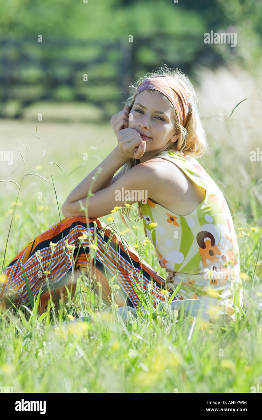 Young woman sitting in field, smiling at camera Stock Photo - Alamy