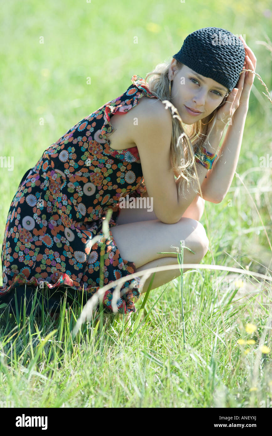 Young woman crouching in field, looking at camera, side view Stock ...