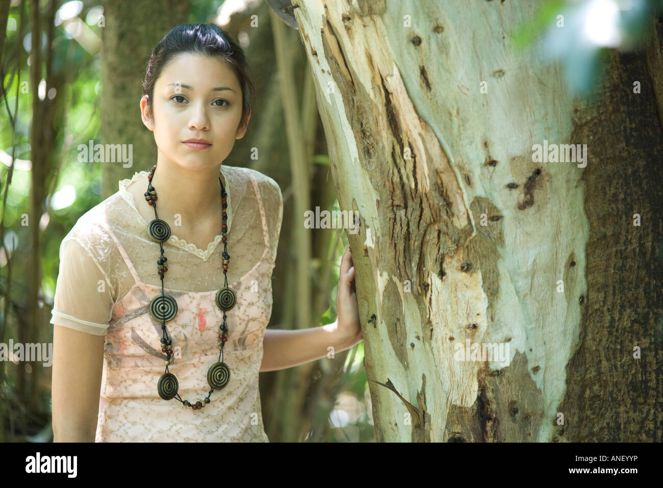 Young woman standing next to tree, looking at camera Stock Photo - Alamy