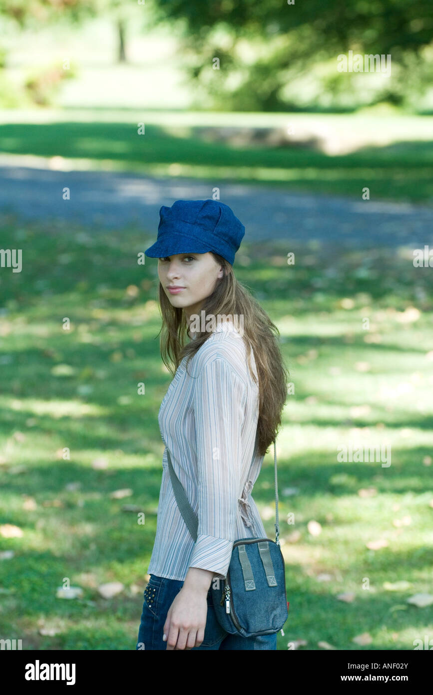 Young woman walking through park, wearing cap, looking over shoulder at ...