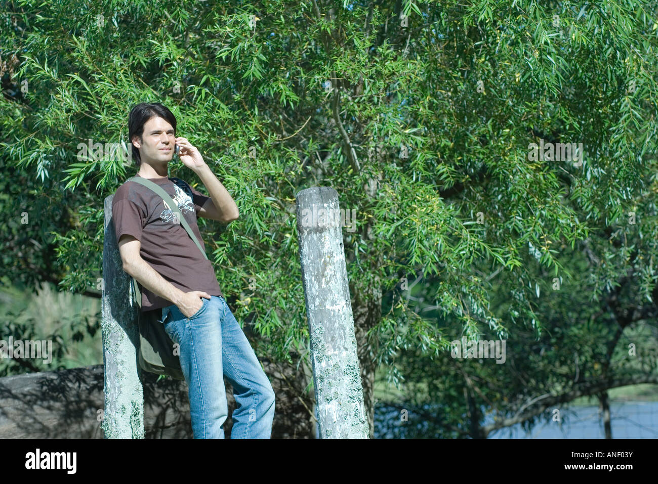 Casual man leaning against post, using cell phone Stock Photo - Alamy