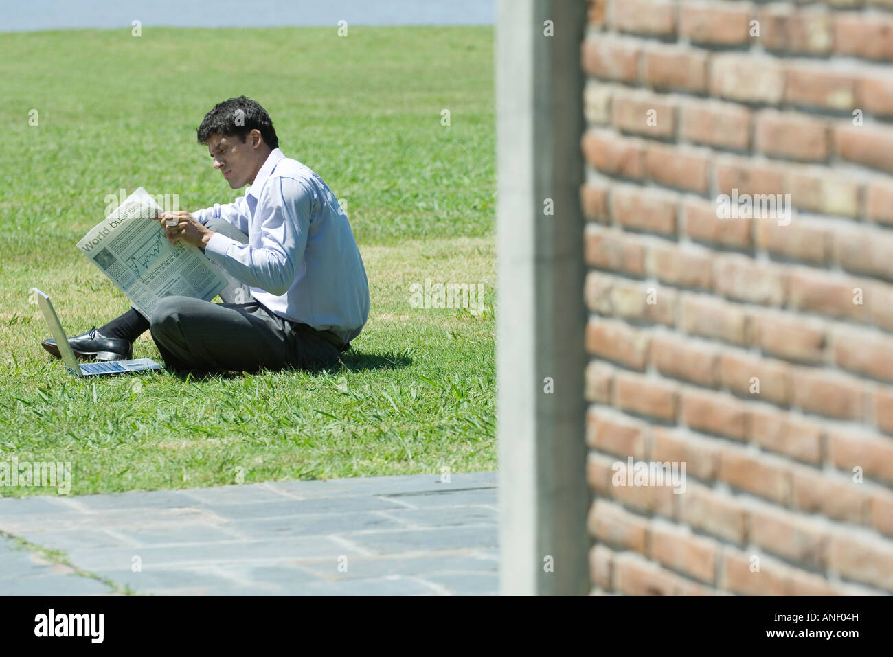 Businessman sitting on ground with laptop, reading newspaper Stock ...