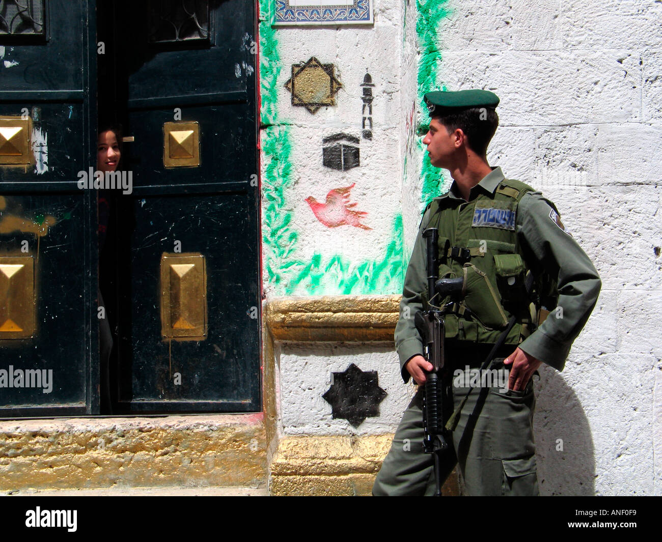 A young Palestinian girl peeps out from a door and looks at an armed ...